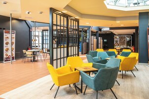 Um restaurante moderno com cadeiras amarelas e azul-esverdeadas, uma mesa de madeira e um teto alto com iluminação embutida.