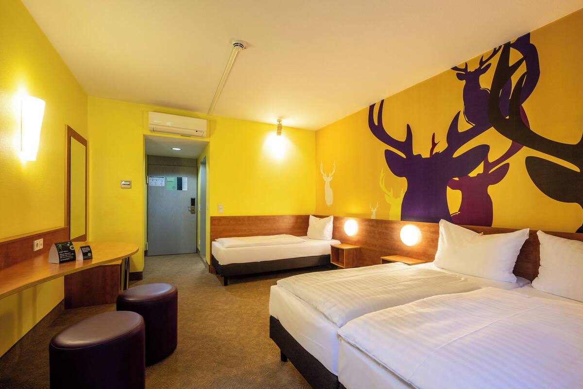 Quarto de hotel com duas camas, uma escrivaninha e um mural na parede.