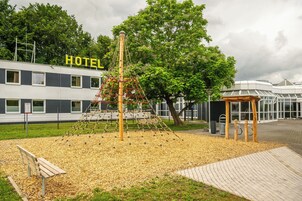 Um parquinho com uma estrutura de escalada e um banco, um gazebo e um prédio de hotel ao fundo.