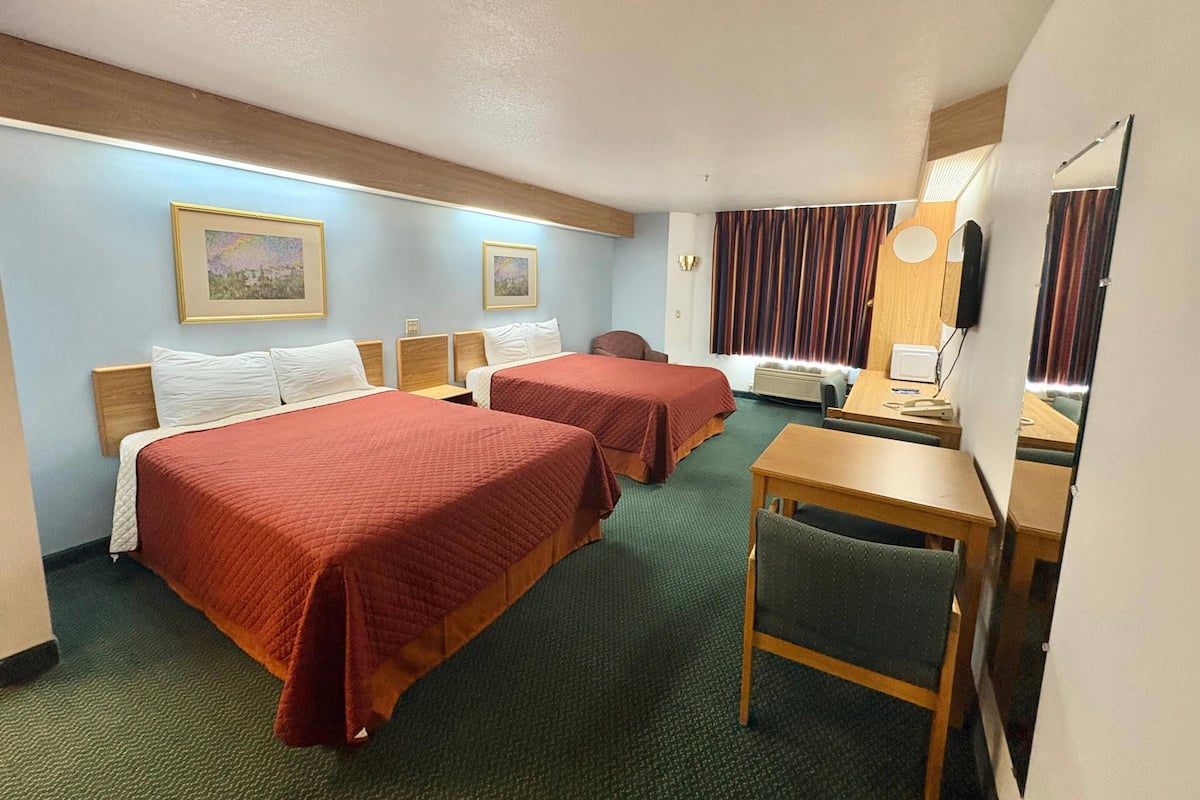 Quarto de hotel com duas camas, uma escrivaninha, uma cadeira, uma televisão e uma janela com cortinas.