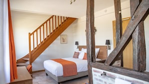 Quarto com escada de madeira, cama com roupa de cama branca e detalhes em laranja, lareira de tijolos e porta de madeira.