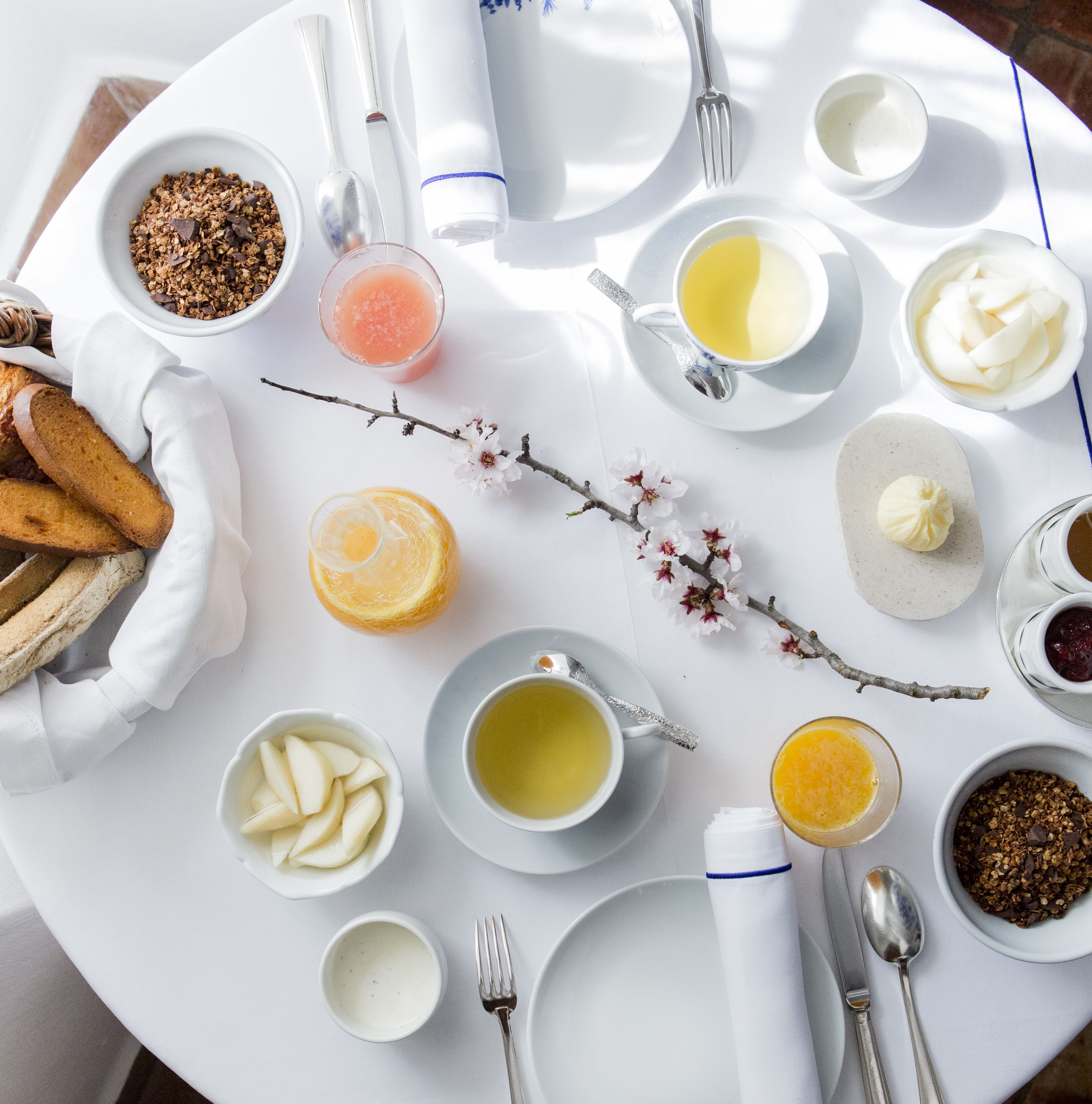 Uma mesa redonda com diversos itens de pequeno-almoço, incluindo pão, fruta e bebidas.