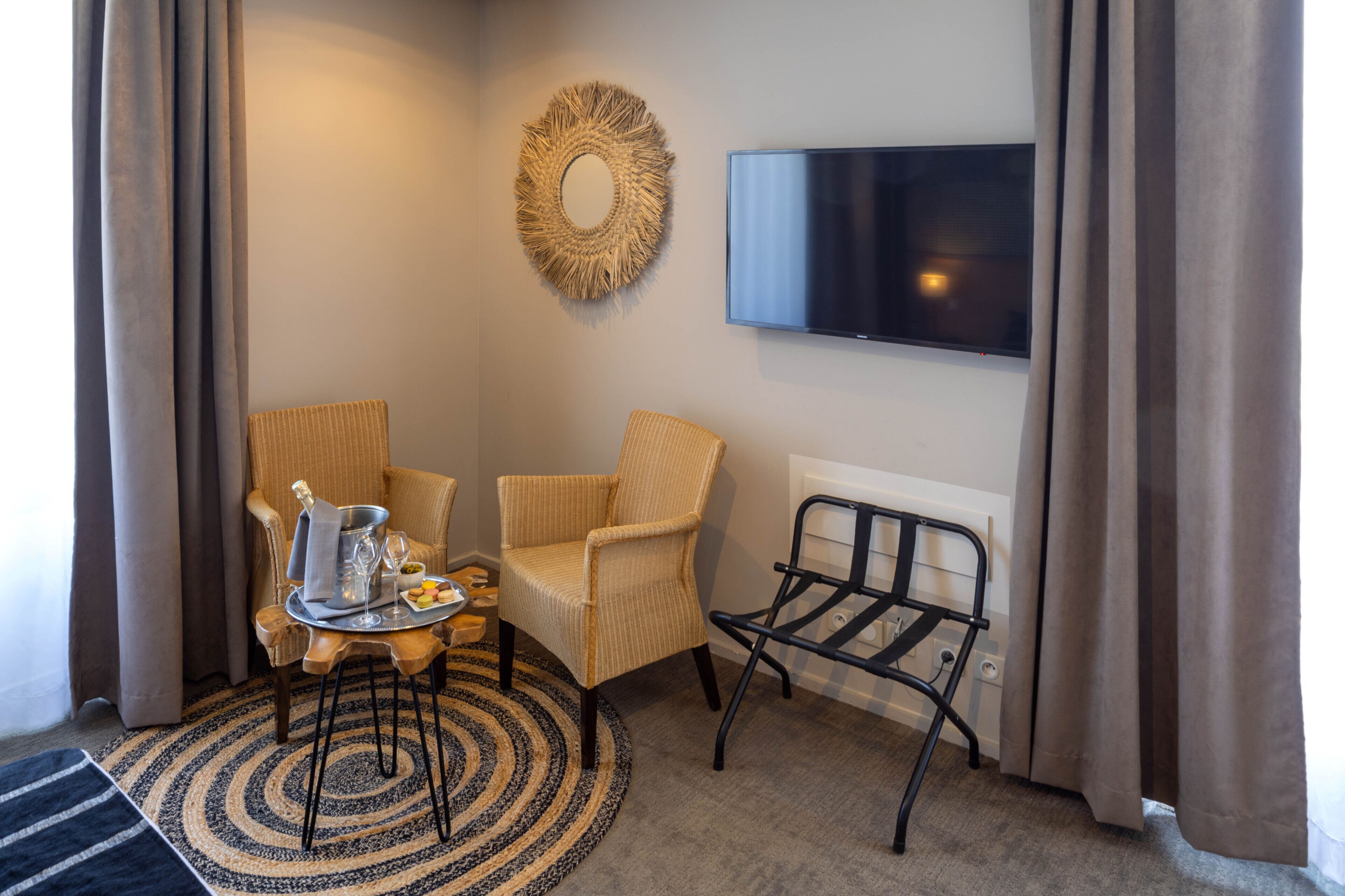 Quarto aconchegante com uma mesa redonda, duas cadeiras, uma TV e um objeto decorativo na parede.