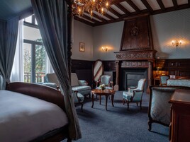 Quarto com cama grande, vários poltronas, lareira e lustre.