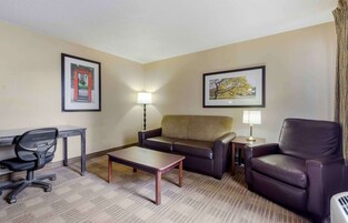 Quarto de hotel com sofá, escrivaninha, cadeira, mesa de centro e duas luminárias.
