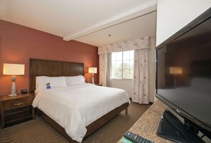 Quarto de hotel com uma cama grande, duas mesas de cabeceira com luminárias, uma televisão de tela plana e uma janela com cortinas.