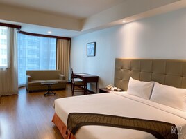 Quarto de hotel com uma cama grande, uma escrivaninha com telefone, uma cadeira e um sofá.
