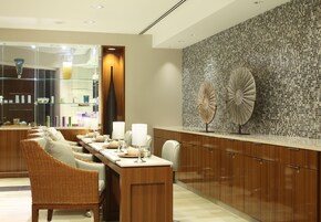 Um hall de hotel moderno com uma longa mesa de jantar, cadeiras de vime, uma vitrine de vidro e uma parede decorativa com azulejos em mosaico.