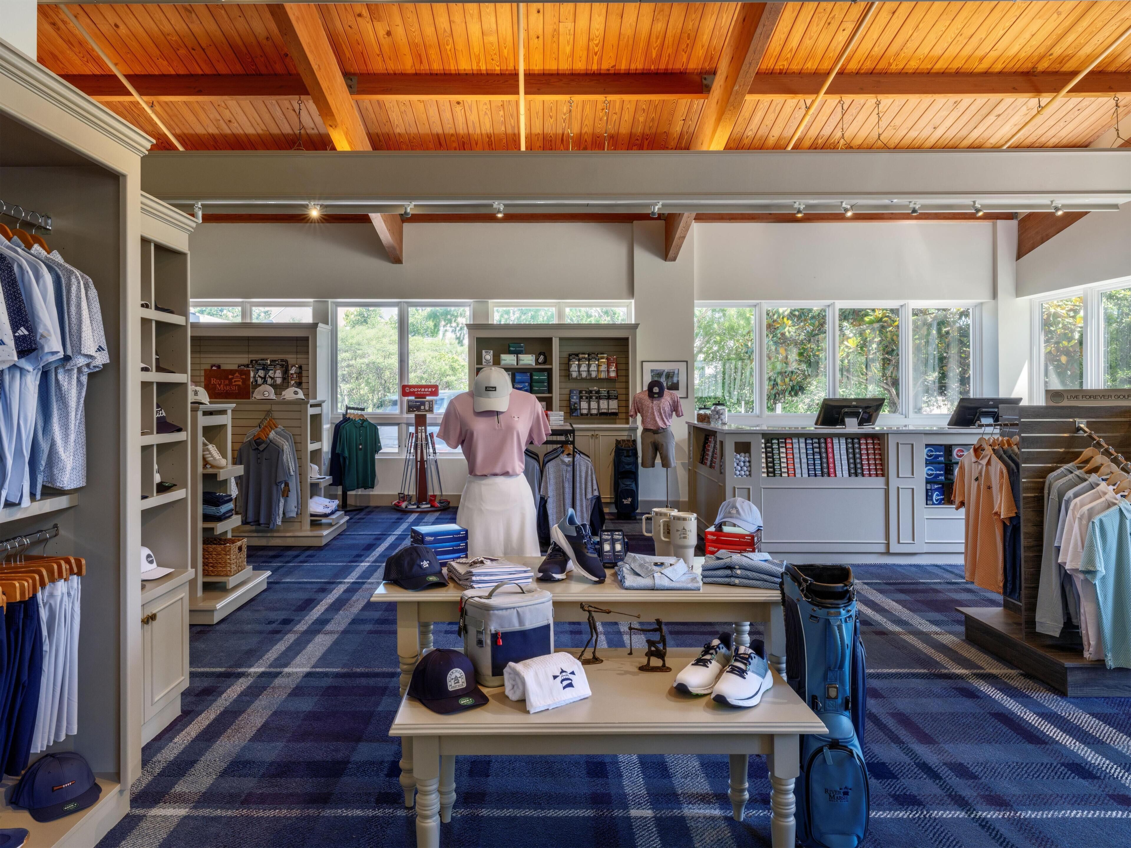 Interior de uma loja de golfe, com prateleiras de vestuário, um manequim e uma mesa com sacos e sapatos de golfe.
