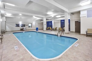 Piscina interior com sinalização clara, chão em azulejo e área de estar com cadeiras e mesas.