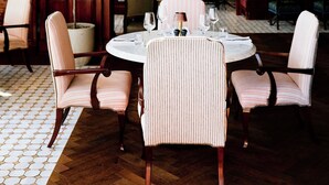 Interior de restaurante com painéis de madeira, cadeiras listradas, samambaias pendentes e uma mesa redonda posta para refeição.