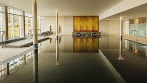Piscina interna com paredes de vidro transparente, um elemento aquático central e piso revestido de azulejos.