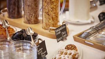 Uma mesa de buffet com diversos alimentos e recipientes, incluindo cereais, frutos secos e doces.