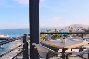 Uma varanda com vista para o mar, uma mesa com cadeiras e um corrimão.