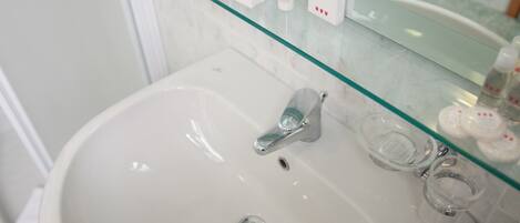 Casa de banho com lavatório branco, prateleira de vidro com produtos de higiene e espelho.
