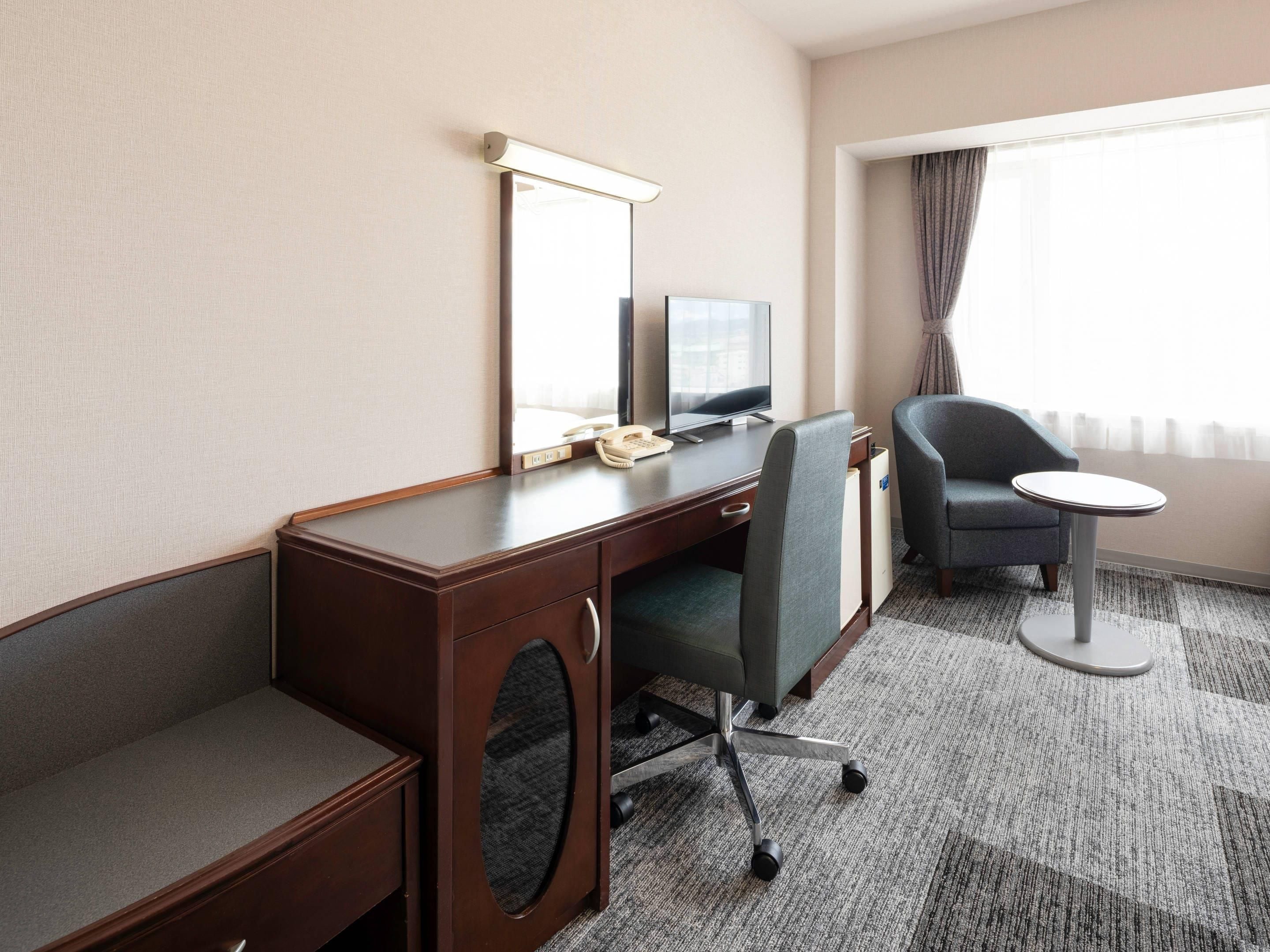 Quarto de hotel com escrivaninha, cadeira e uma pequena mesa redonda.