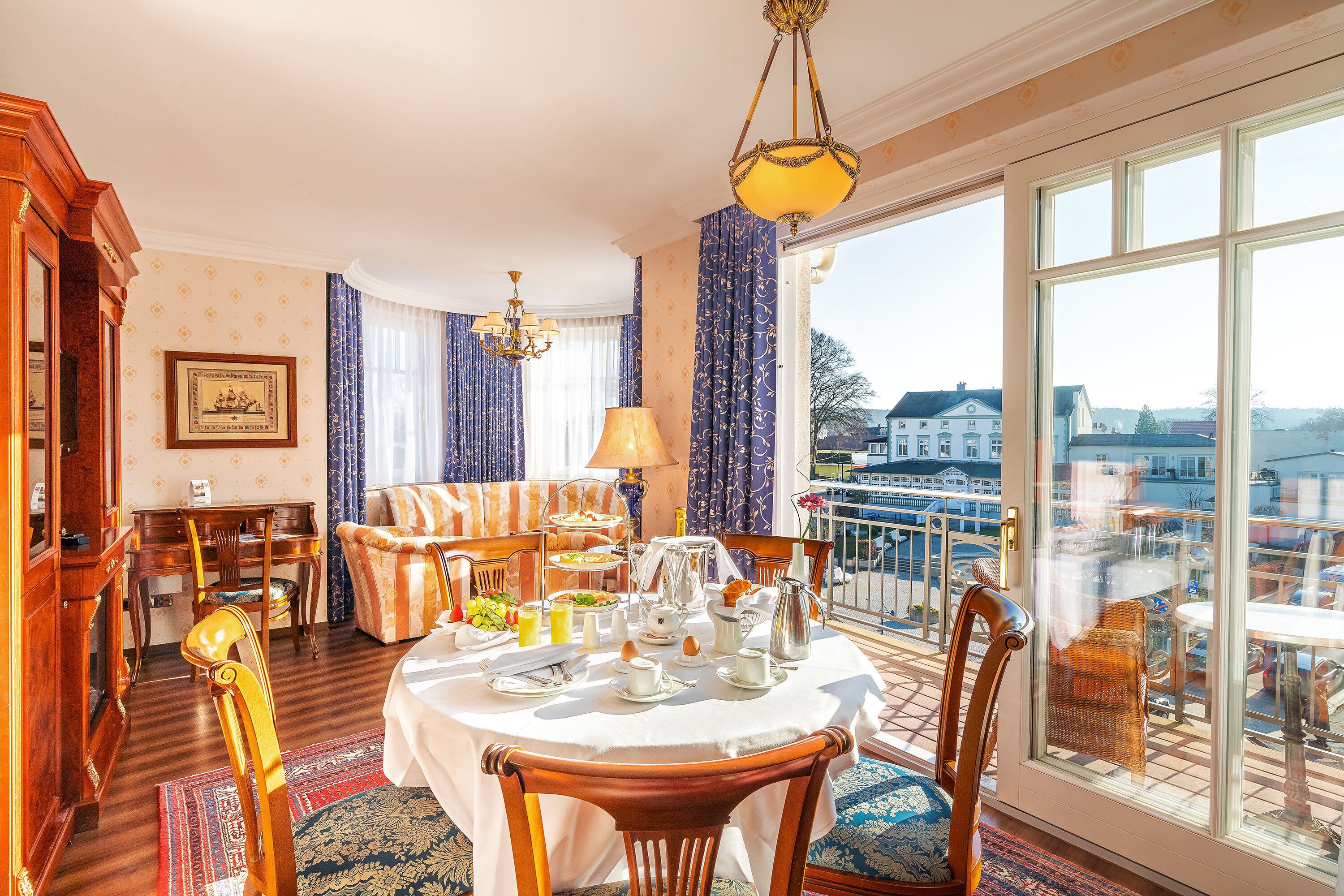 Uma área de refeições com uma mesa posta para o café da manhã, um sofá e vista da cidade através de grandes janelas.