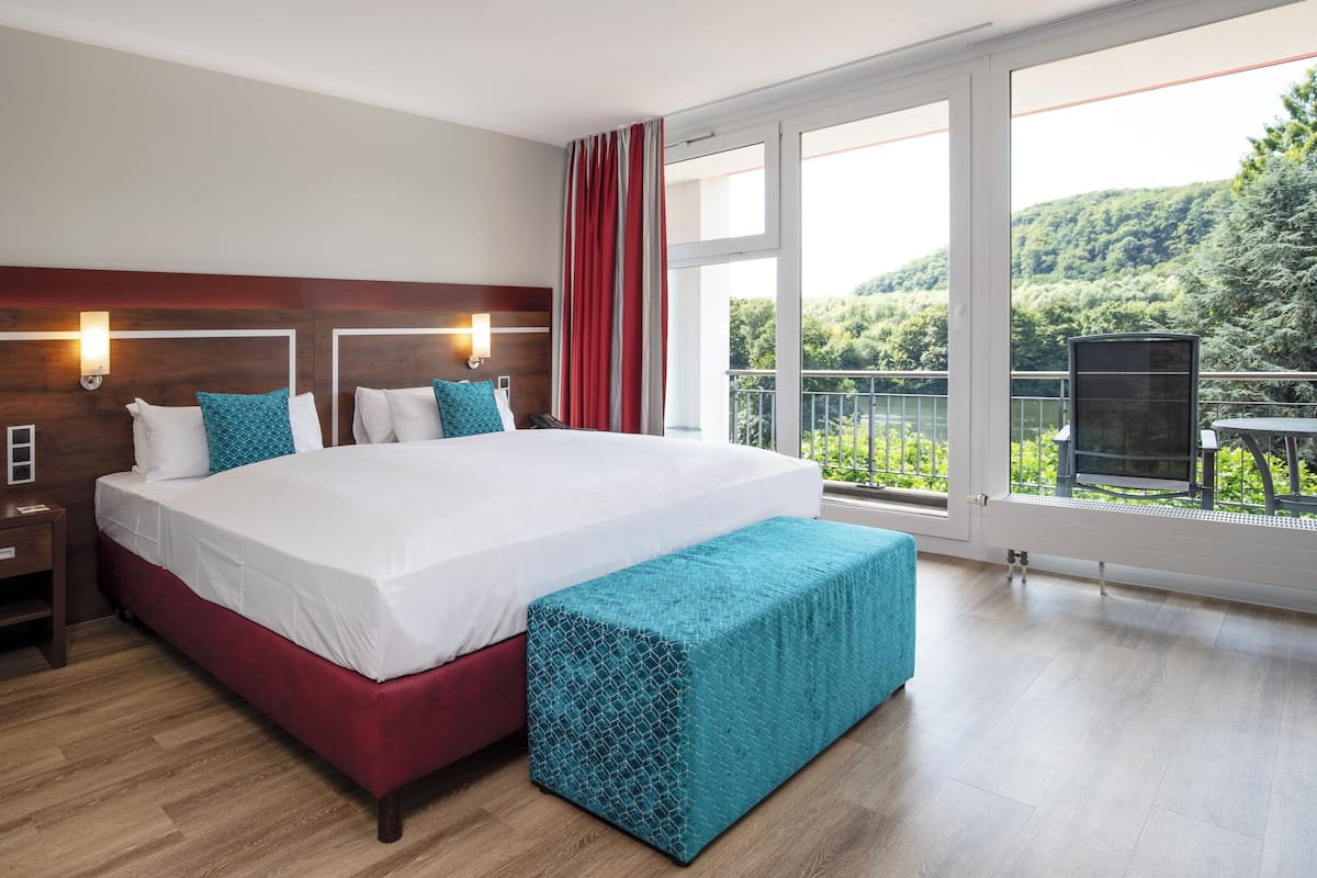 Quarto de hotel moderno com uma cama grande, cabeceira de madeira e uma varanda com vista panorâmica.