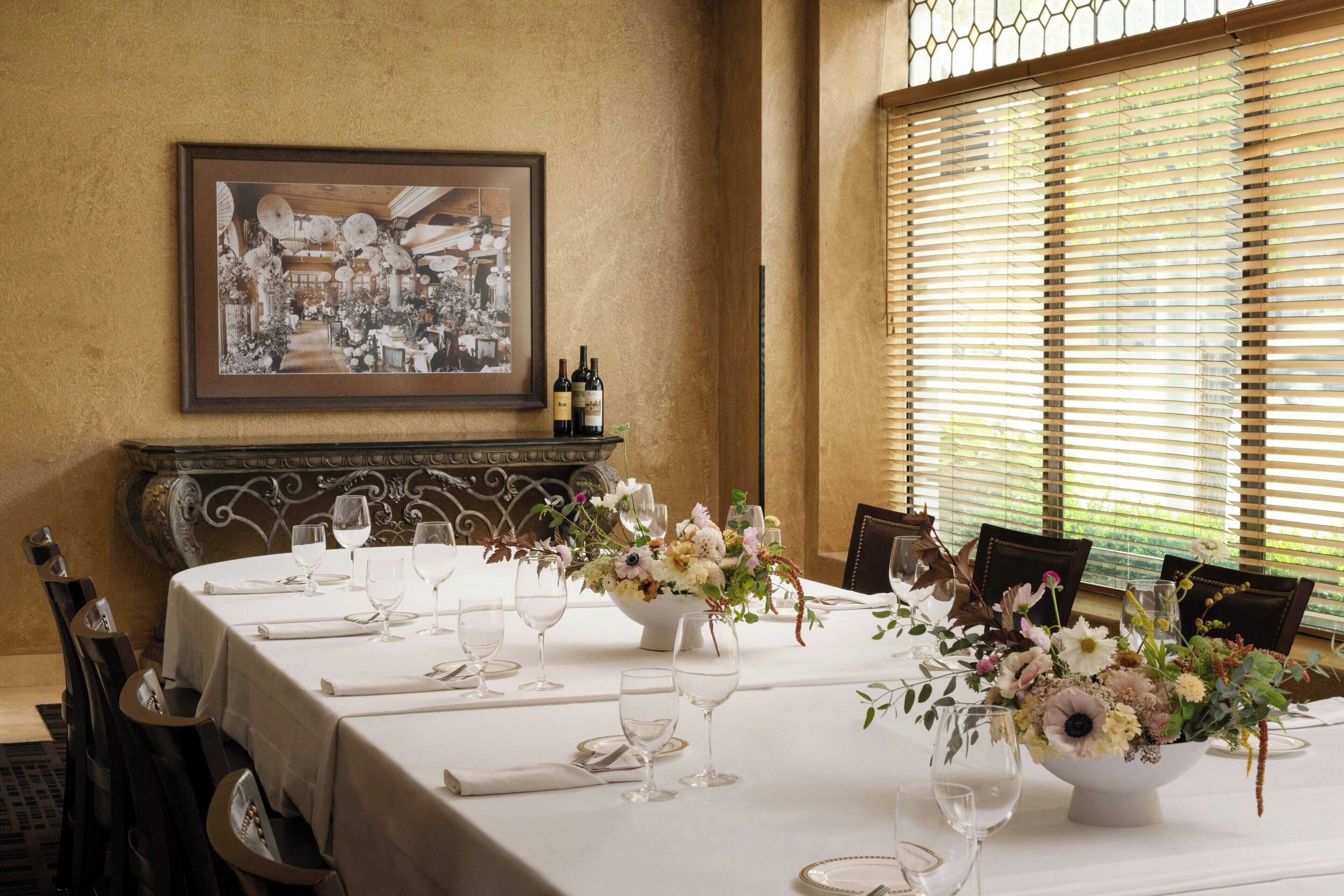 Uma mesa de jantar posta com toalhas brancas, copos de vinho e arranjos florais.