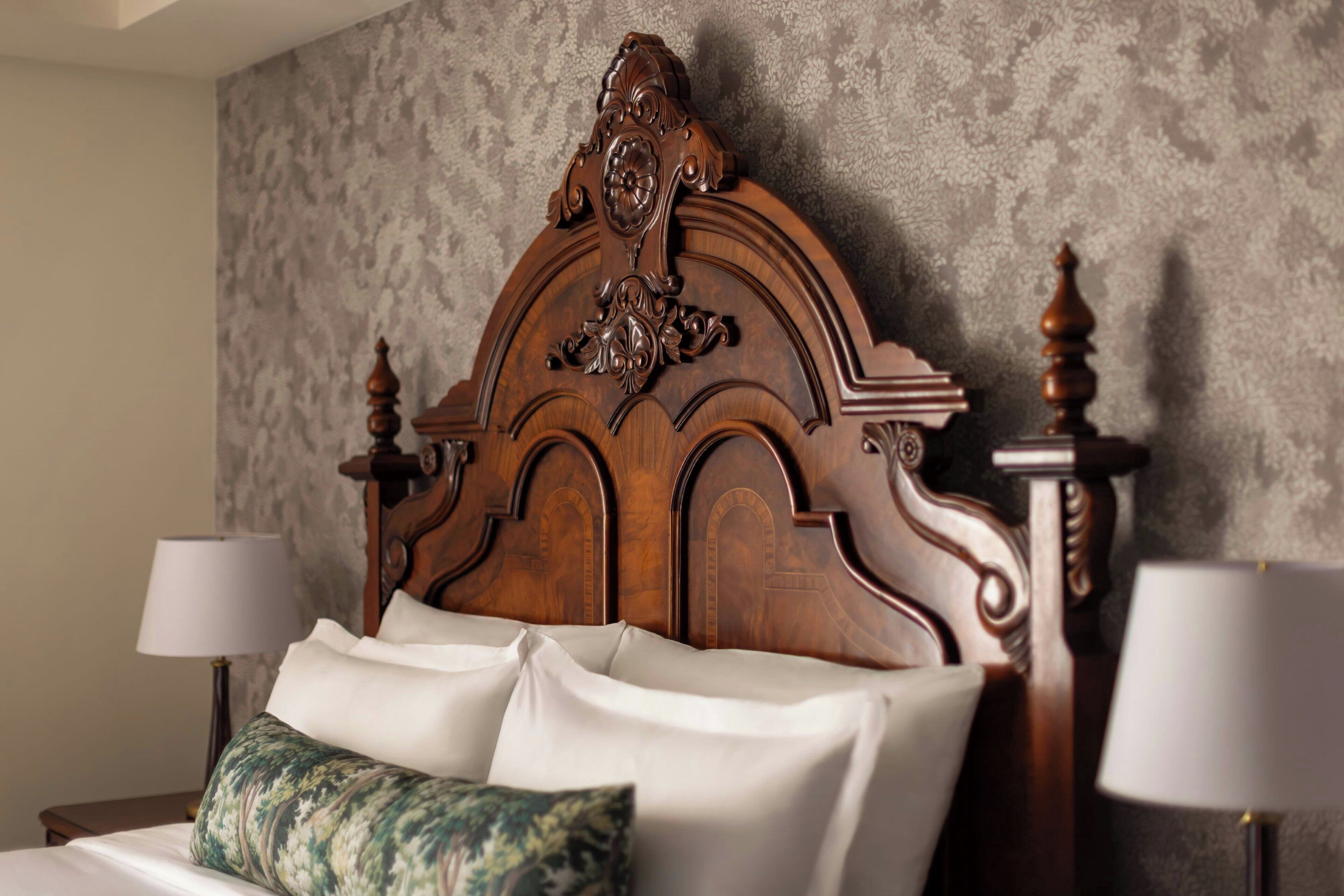 Uma cama com cabeceira de madeira, duas luminárias de apoio e um travesseiro estampado.
