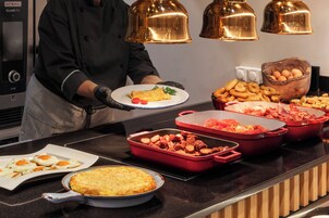 Uma mesa de buffet com diversos alimentos, incluindo um prato de ovos, um refritário e recipientes com carne.