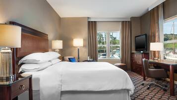 Quarto de hotel com uma cama grande, uma escrivaninha, uma cadeira, uma TV e uma janela com vista para o exterior.