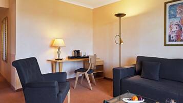 Uma sala de estar moderna com um sofá, duas poltronas, uma mesa de centro com frutas, um abajur e uma escrivaninha com uma cadeira.