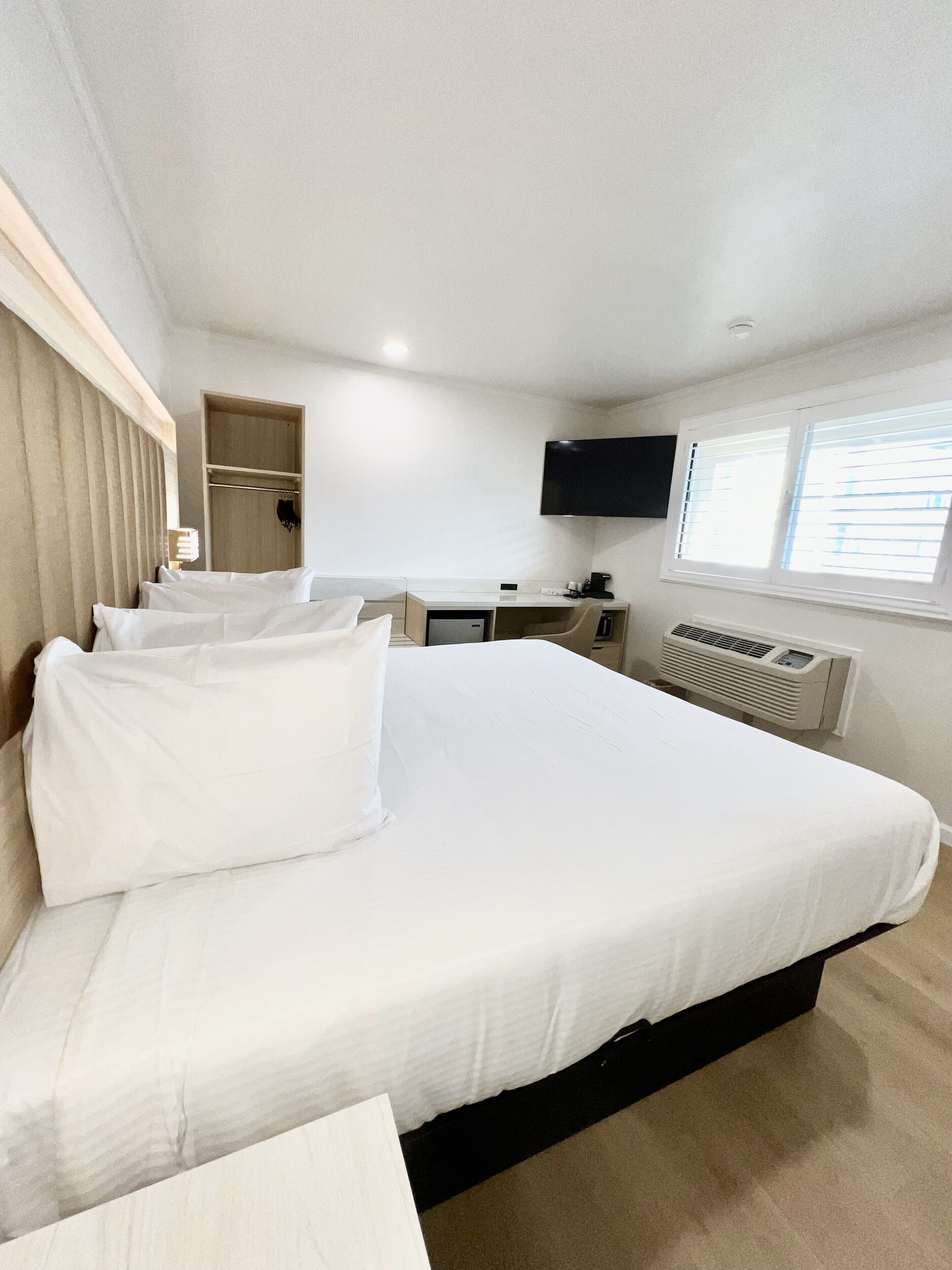 Quarto de hotel com uma cama grande, uma escrivaninha, uma cadeira, uma televisão e uma janela.