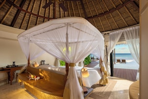 Quarto com cama de dossel, vista para a praia e um deck de madeira.