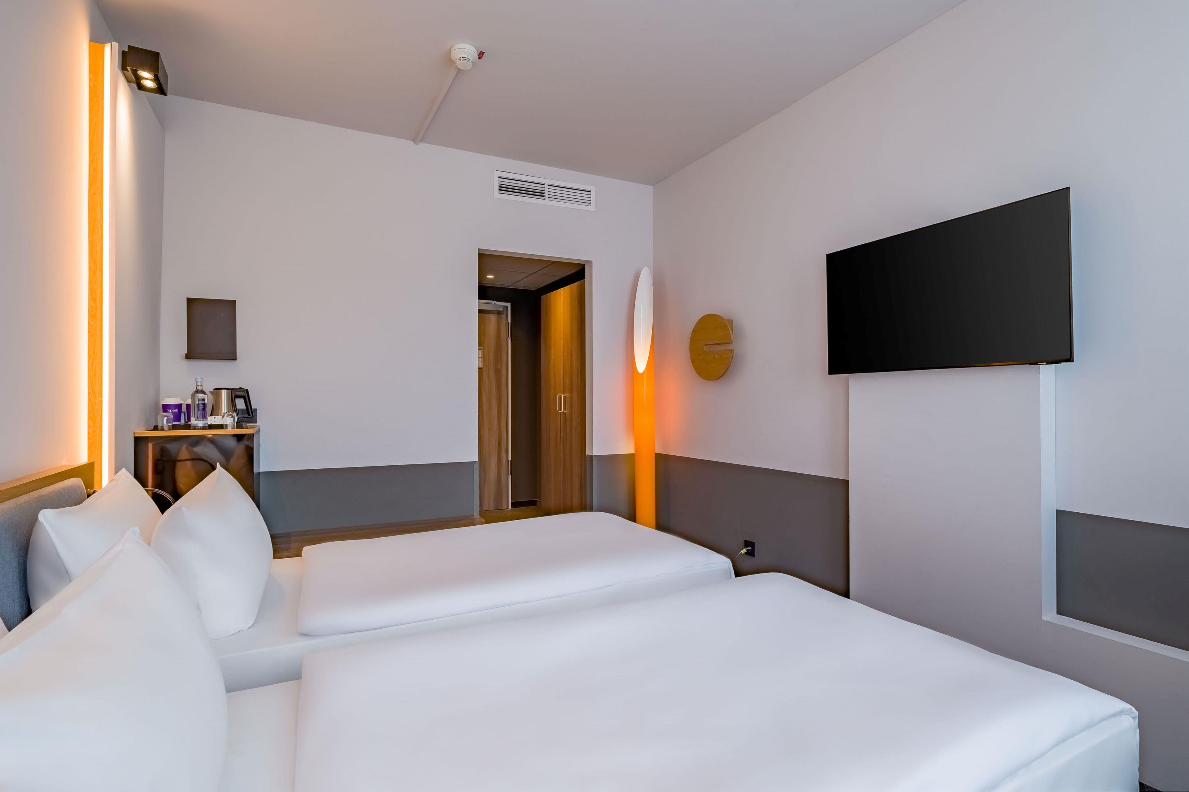 Quarto de hotel com uma cama, uma televisão na parede e uma mesa de cabeceira com abajur.