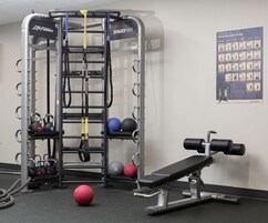 Uma academia com barra de exercícios, kettlebells, bolas medicinais e aparelho de supino.