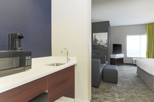 Quarto de hotel com cozinha compacta, incluindo micro-ondas, pia e máquina de café. Há uma cama, uma televisão e uma janela com cortinas.