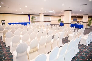 Uma sala de conferências com fileiras de cadeiras brancas, uma mesa azul com arranjos florais e um pódio com a inscrição 'PEGAUSUS'.