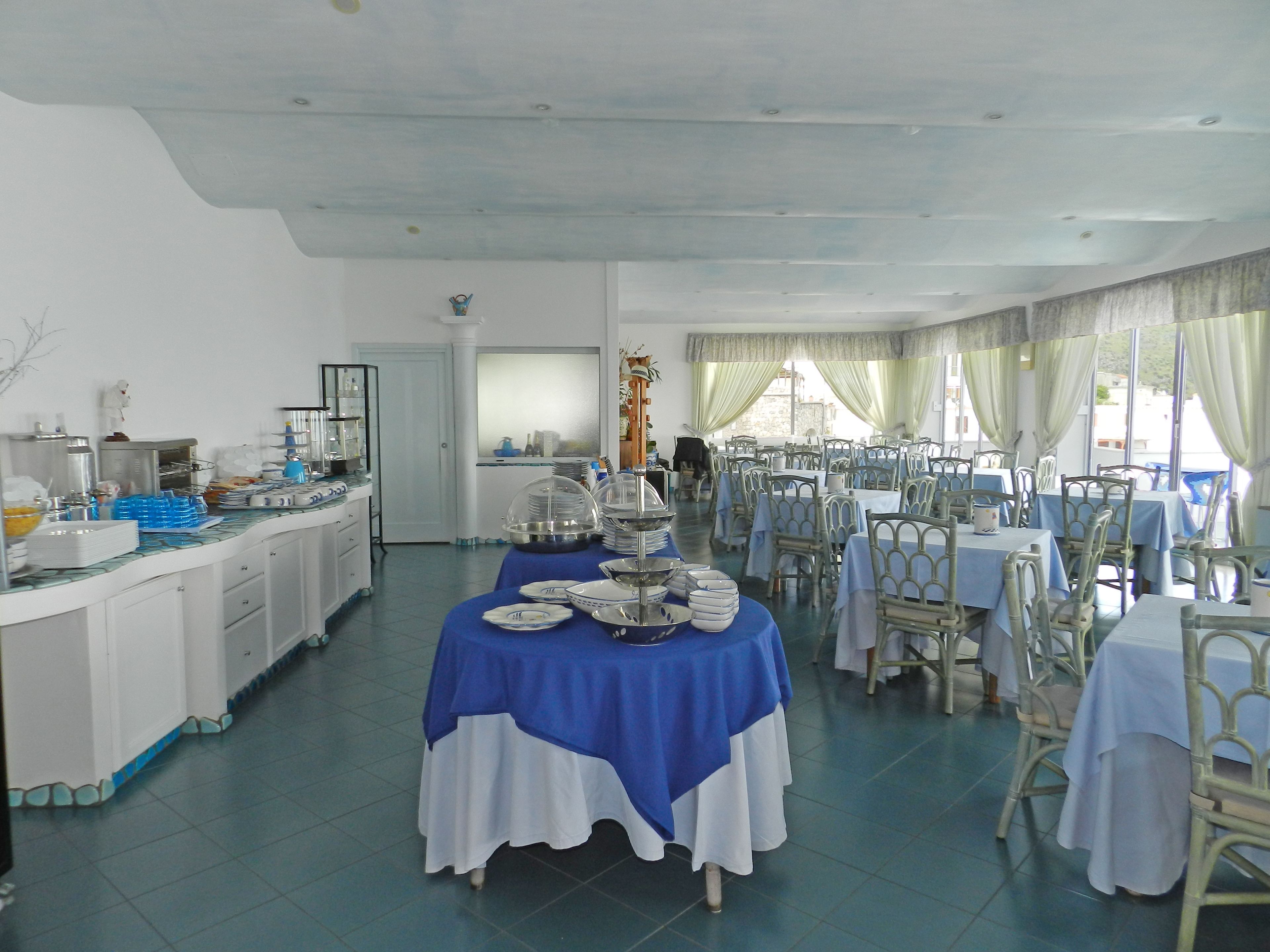 Uma ampla área de refeições com mesas postas, um buffet com diversos pratos e vista para o exterior através de grandes janelas.