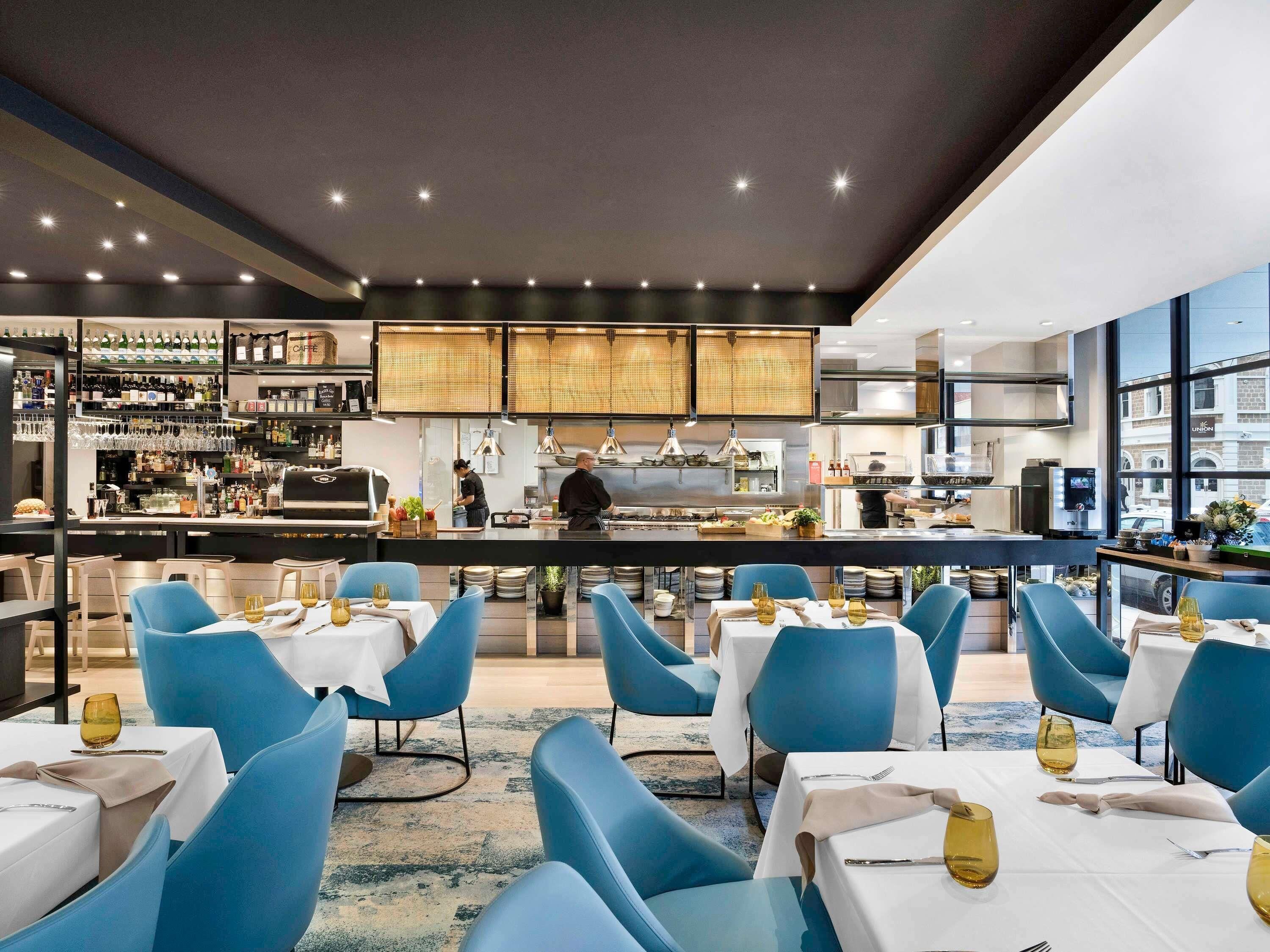 Restaurante moderno com cadeiras azuis, mesas brancas e um espaço de bar.