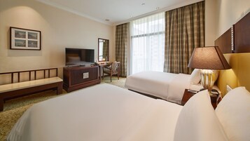 Quarto de hotel com duas camas, uma escrivaninha, televisão e janela com cortinas.