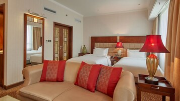 Quarto de hotel com sofá, duas camas, mesa de cabeceira, luminária e espelho.