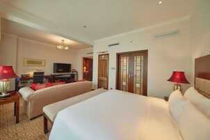 Quarto de hotel com duas camas, uma escrivaninha, uma televisão e um abajur vermelho.