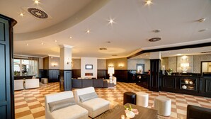 Um hall espaçoso com piso xadrez, área de estar com sofás, balcão de recepção e um espelho grande.