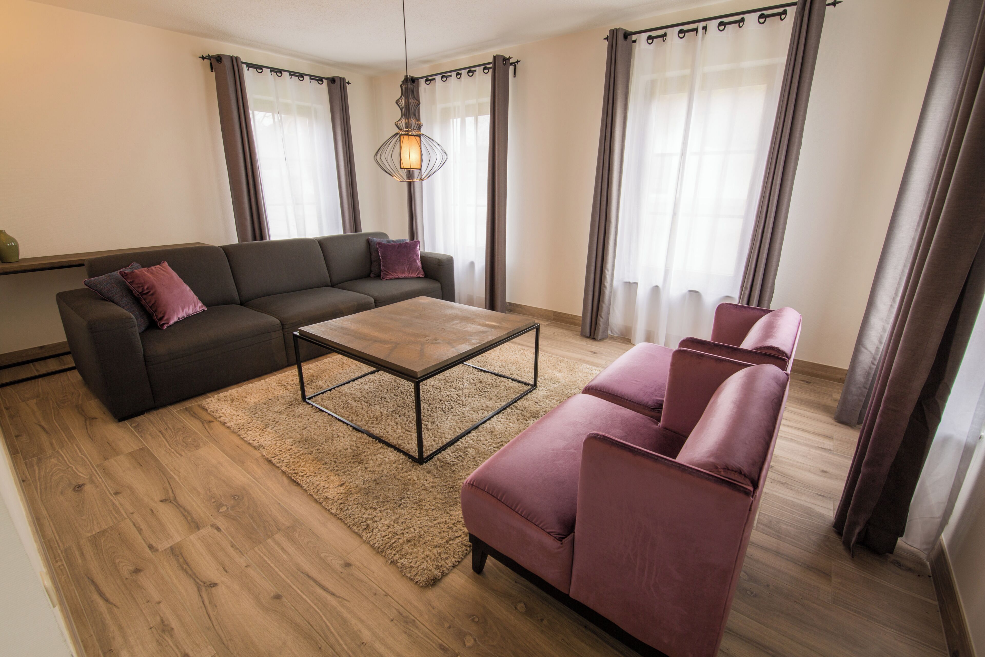 Sala de estar com sofá, poltrona, mesa de centro e cortinas.