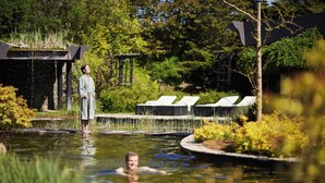 Uma área de piscina com espreguiçadeiras, uma pessoa parada e outra nadando.