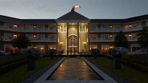 Um hotel com vários andares, entrada central, piscina e uma bandeira no topo.
