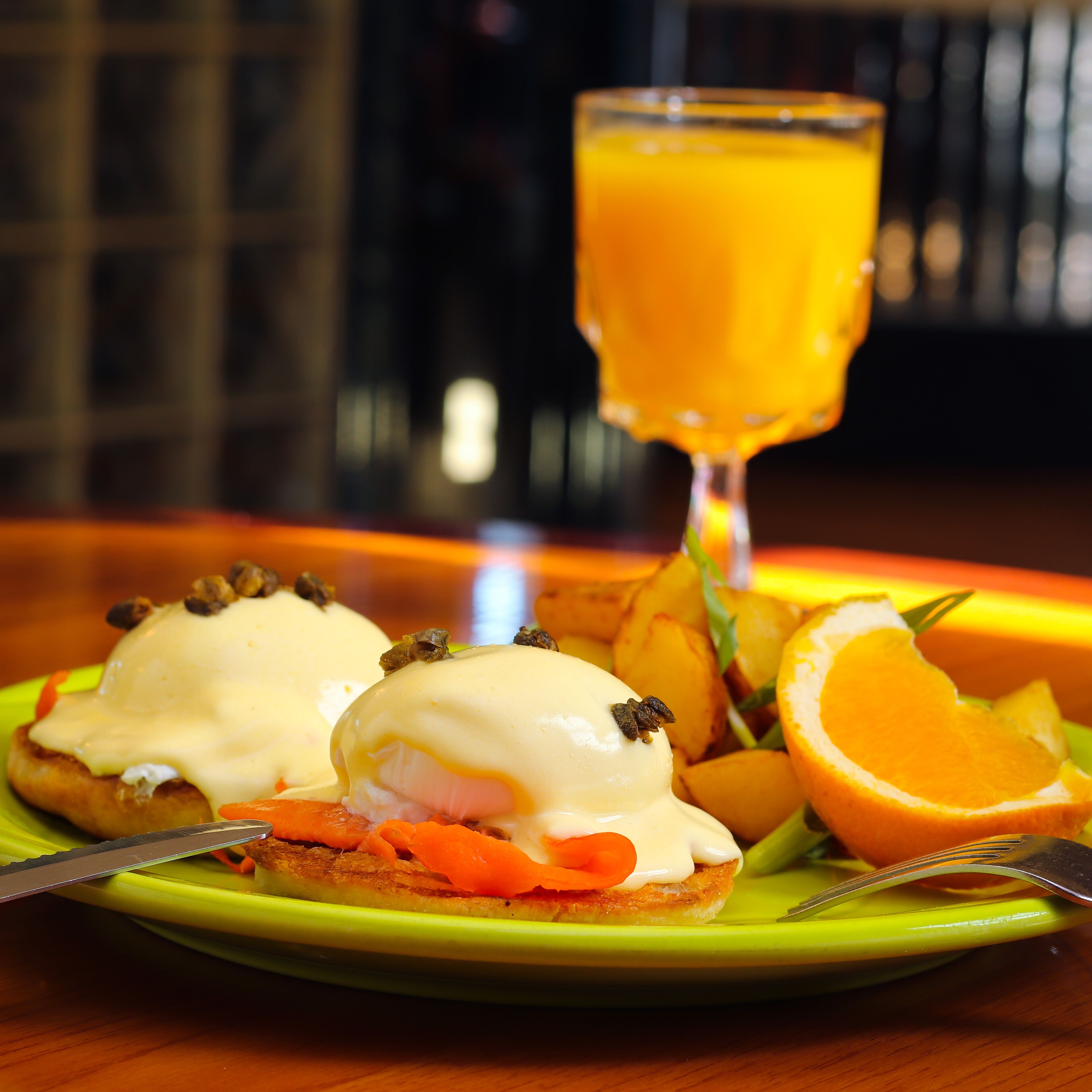 Um prato com ovos Benedict, um copo de suco de laranja e uma fatia de laranja sobre um prato verde.