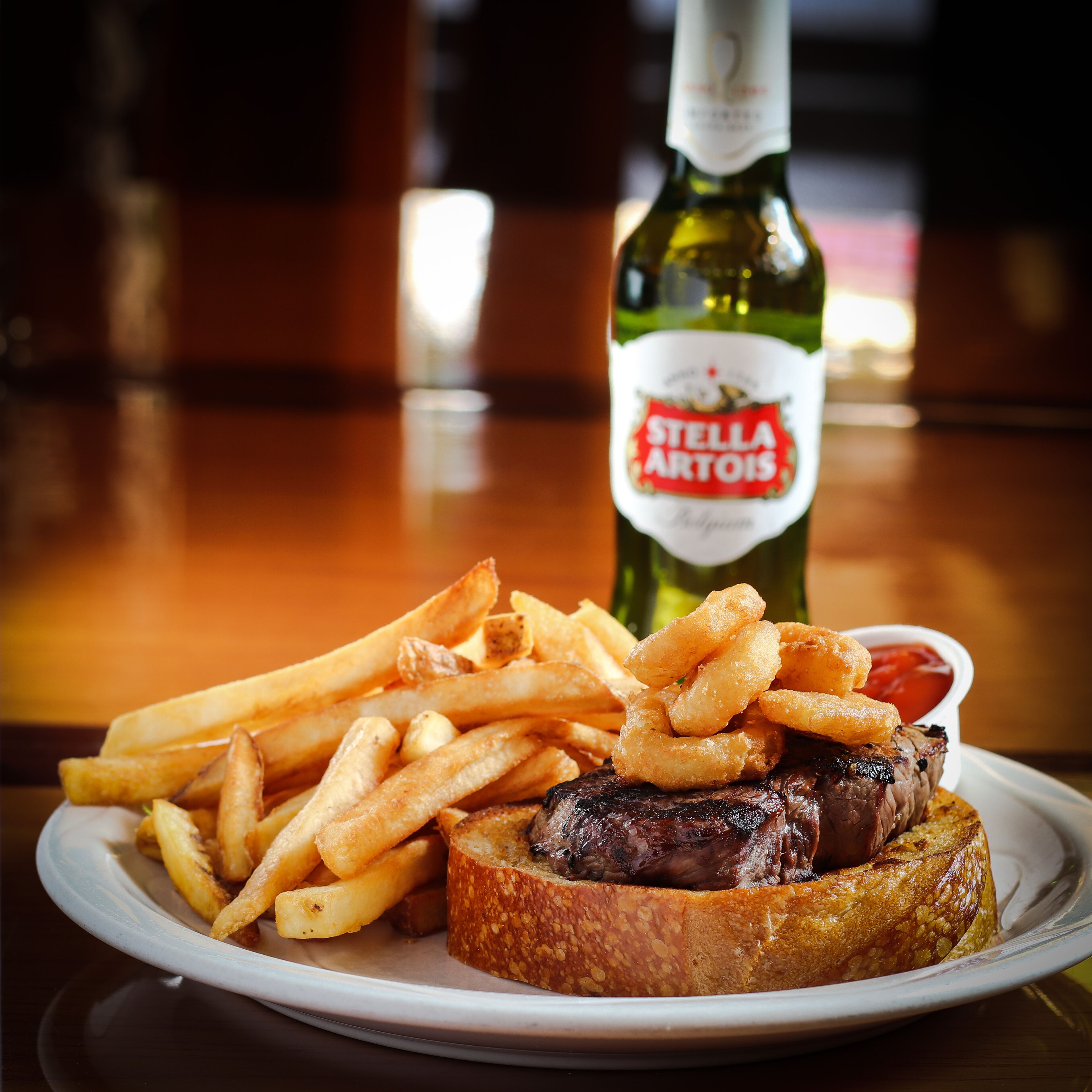 Um prato com bife, batatas fritas e uma garrafa de cerveja Stella Artois.