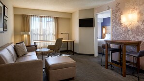 Quarto de hotel com sofá, pufé, escrivaninha e cadeiras.
