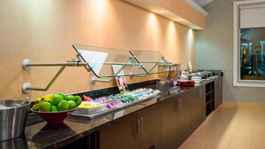 Um balcão de buffet com diversos tipos de comida, uma tigela de maçãs verdes e uma vitrine de vidro.