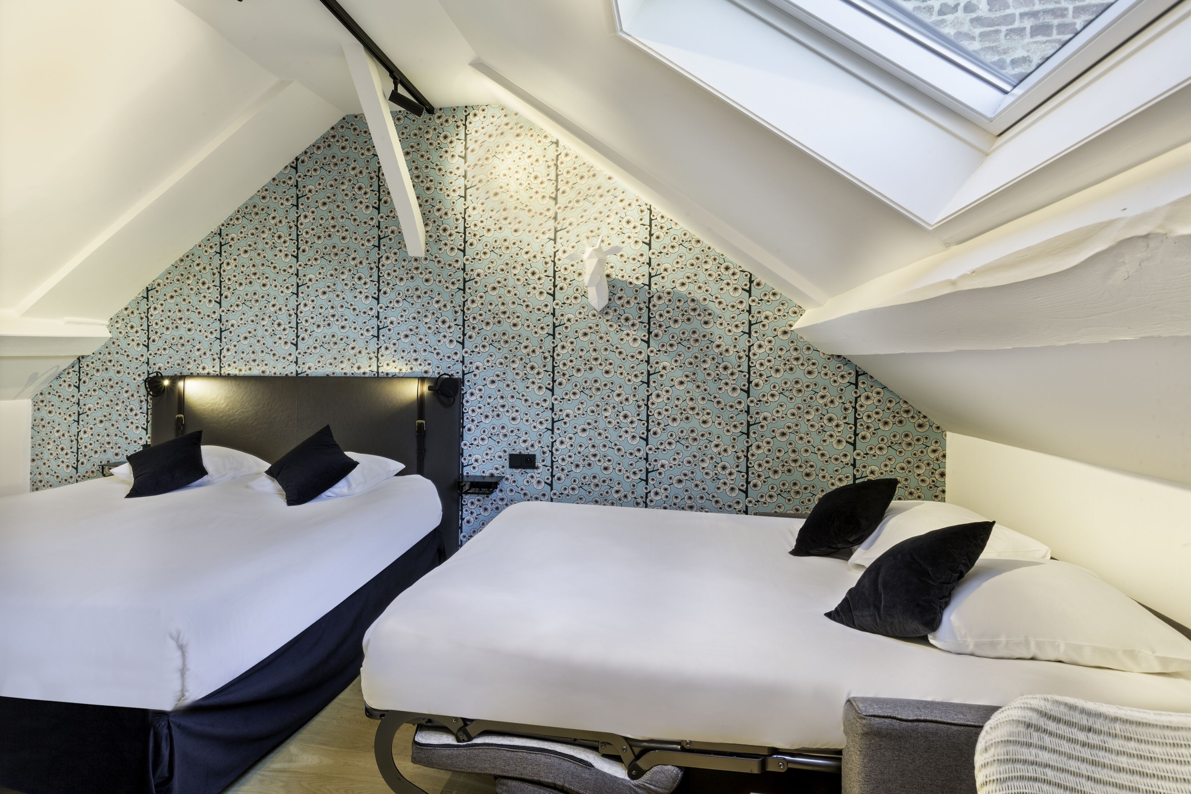 Quarto com duas camas, claraboia e papel de parede estampado.