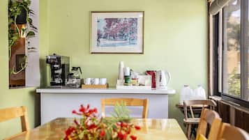 Uma sala de jantar com uma mesa, cadeiras, máquina de café, chaleira e um quadro na parede.