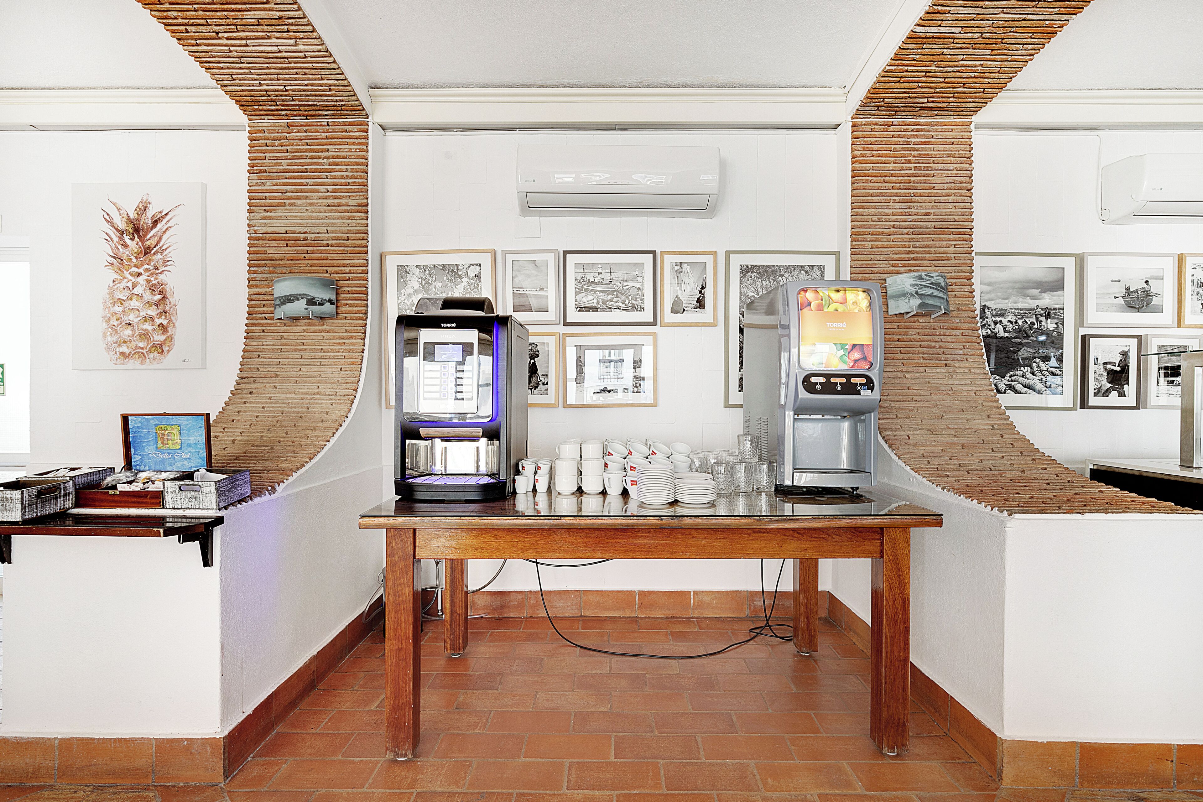 Uma estação de café com máquina de café, dispensador de bebidas e uma mesa com xícaras e pratos.