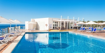 Uma área de piscina com espreguiçadeiras, guarda-sóis e uma piscina.